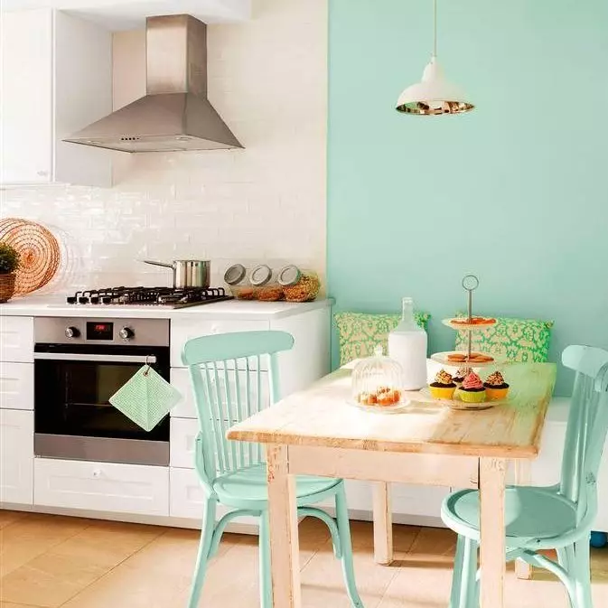 Cuisine blanche et vert menthe avec table à manger en bois, chaises Thonet vertes, plafonnier, hotte aspirante et carrelage blanc brillant