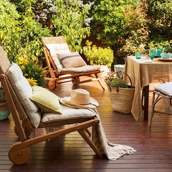 Terras met houten vloer, ligstoelen, eettafel, reiswieg, planten en bomen.