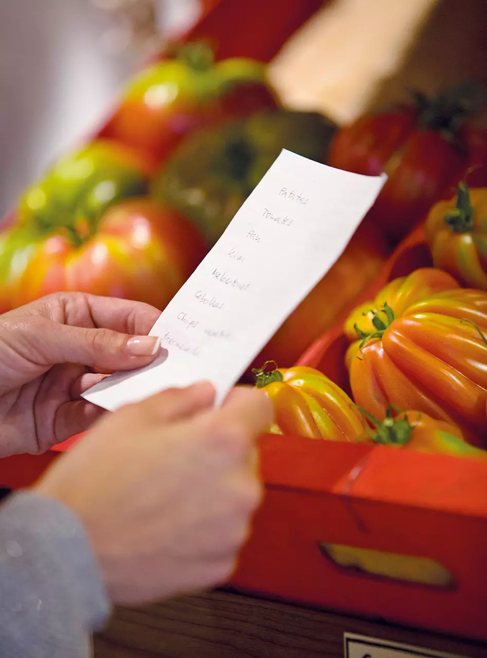 Detail der Hände, die Einkaufsliste und Tomaten im Hintergrund halten