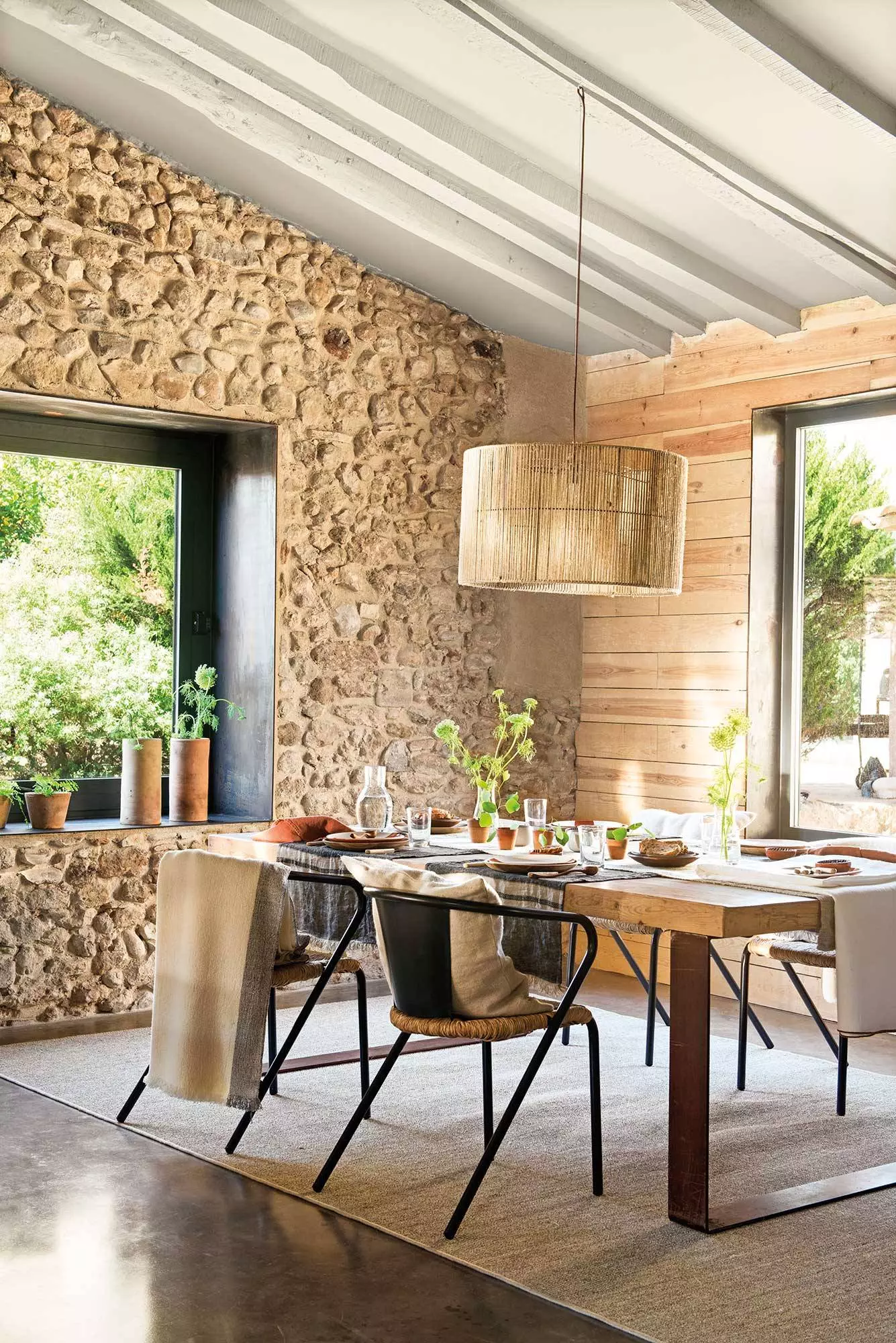 Salle à manger avec murs en pierre et table avec plateau en bois et pieds en fer_00513576