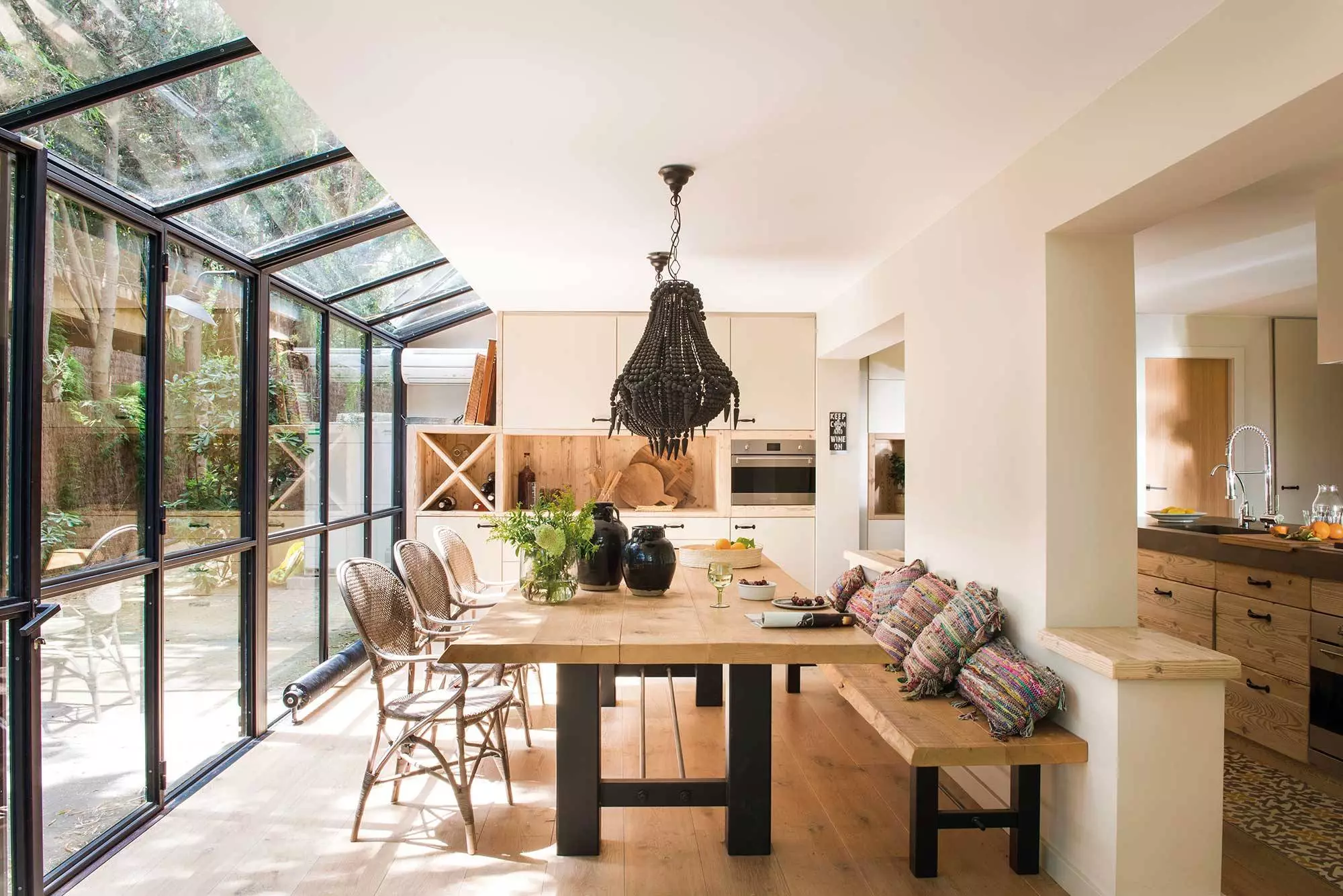 Salle à manger avec grande table en bois et pieds en métal et grande fenêtre sur le jardin