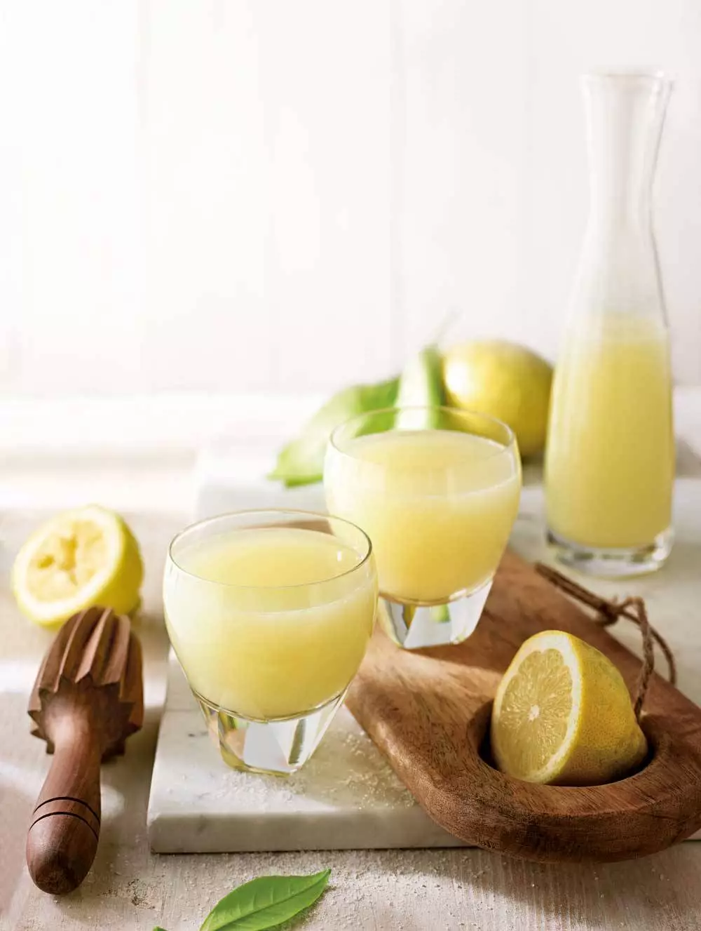 Gelas lan jug karo jus lemon ing meja kayu lan marmer lan lemon pamisah alam