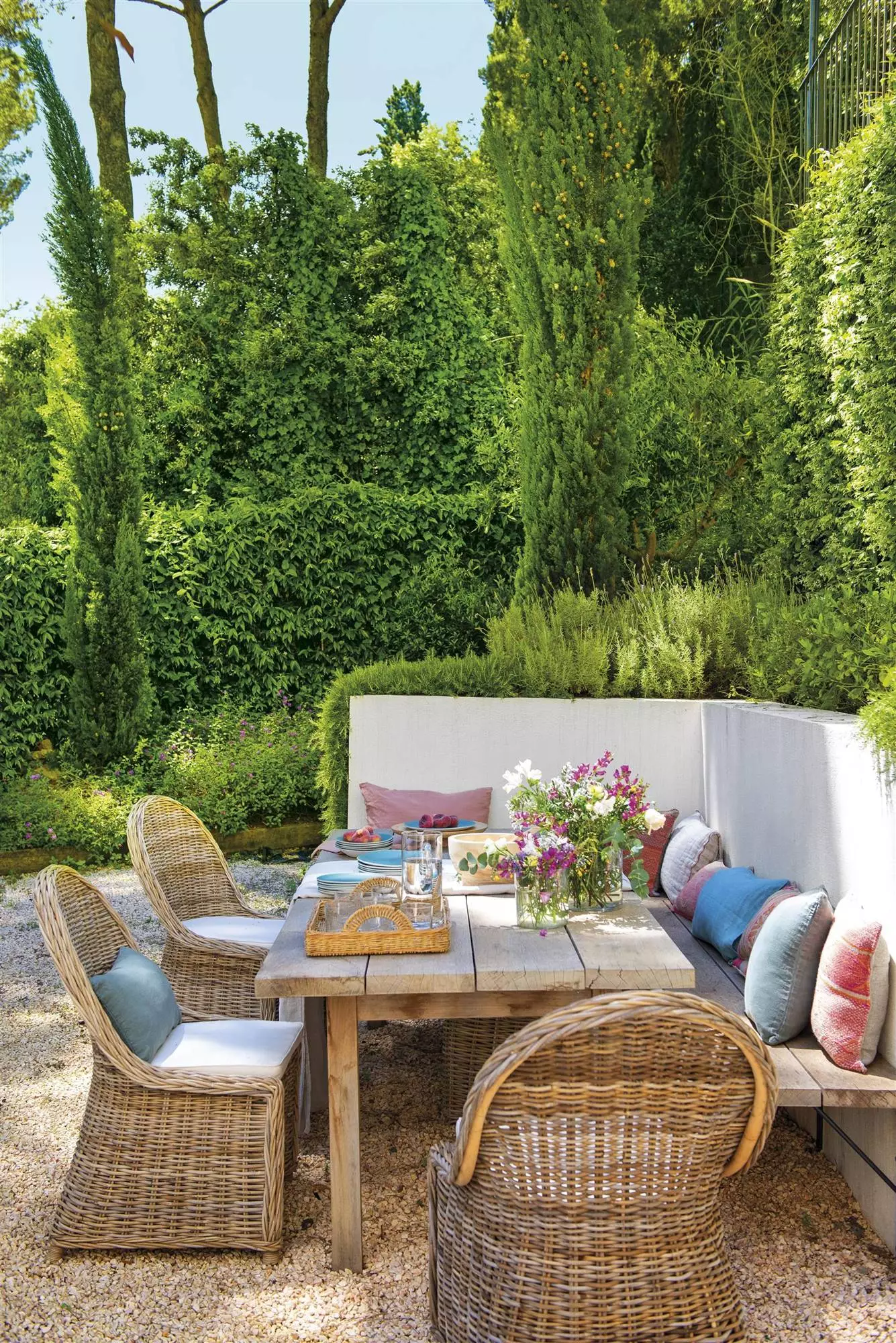 outdoor-dining-room-with-wooden-table-bench-against-the-wall-and-wicker-seats-00527524